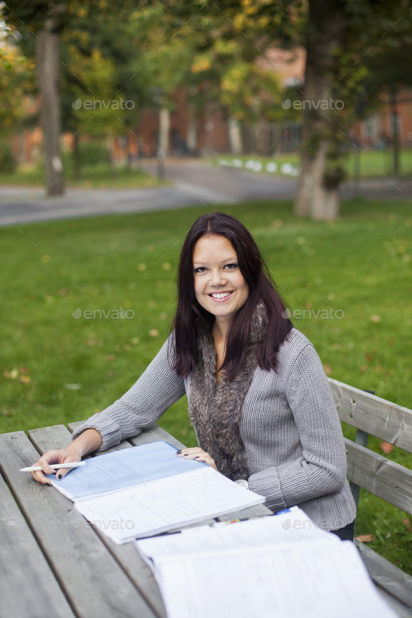 Portrait of beautiful young female student sitting at table while ...