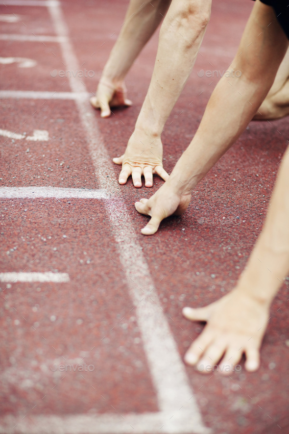 Cropped hands of young athletes leaning on starting line at tracks ...