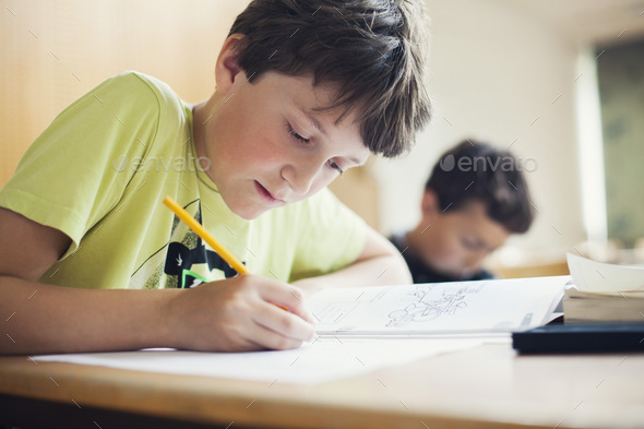 Boy writing in book on desk at school Stock Photo by astrakanimages