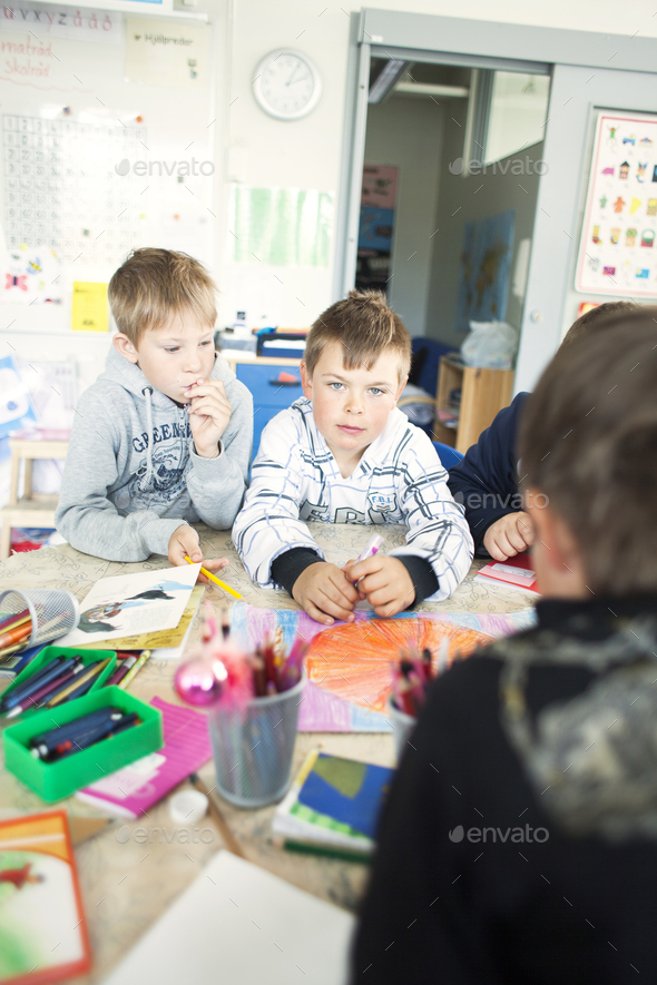 Portrait of schoolboy drawing with classmates at desk in classroom ...