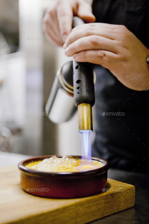 Midsection of chef caramelizing creme brulee with flaming torch at ...