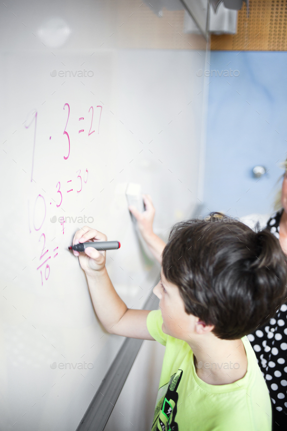 Schoolboy solving mathematics on whiteboard with teacher in classroom ...