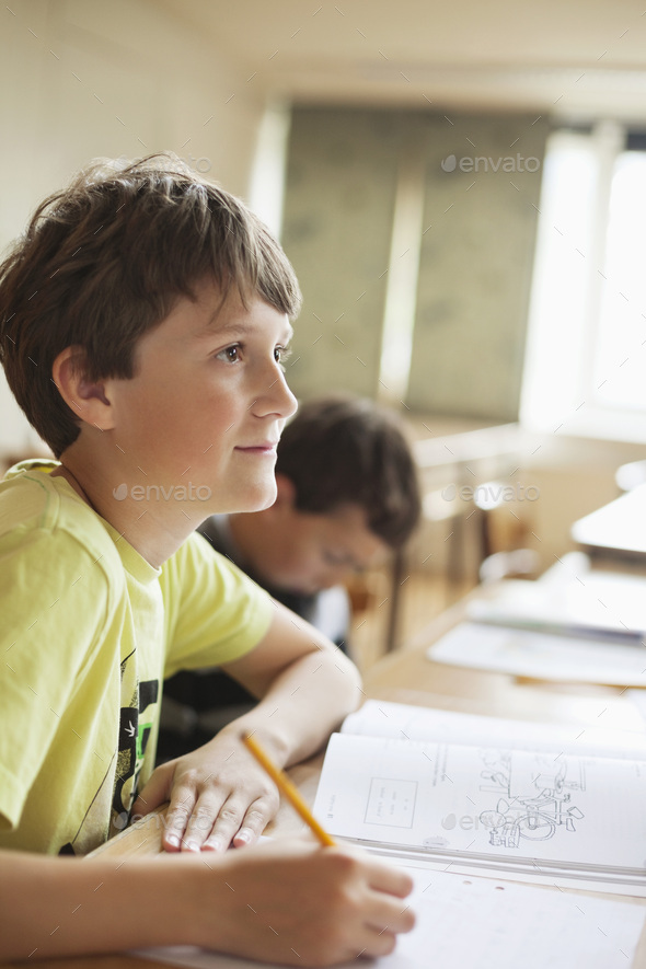 Side view of boy writing in book at school classroom Stock Photo by ...