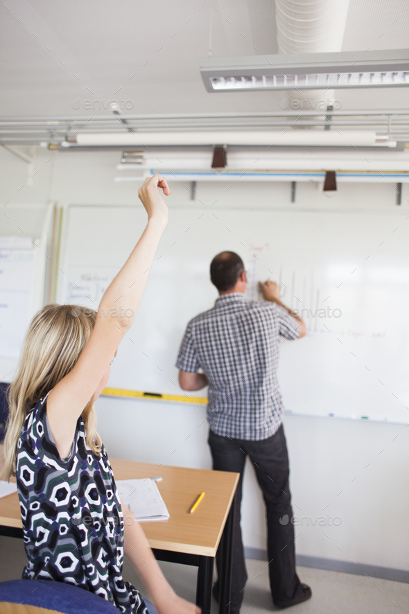 Side view of schoolgirl raising hand while teacher explaining in ...