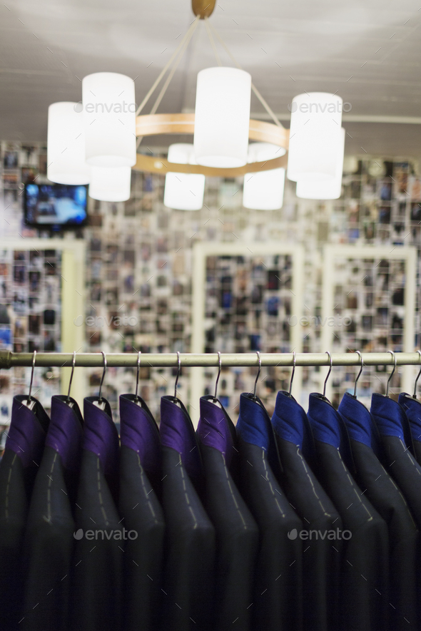 Illuminated pendant light hanging over suit rack in clothing store ...
