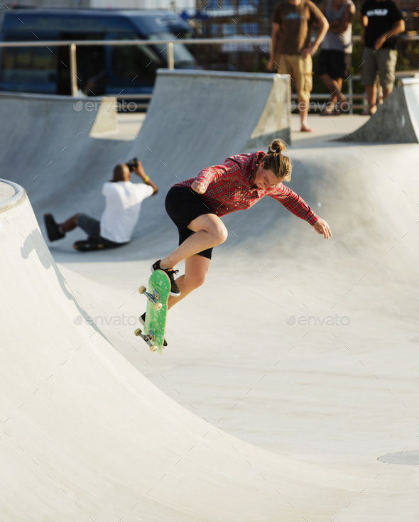 Full length of sporty woman performing stunt on ramp in city skate park ...