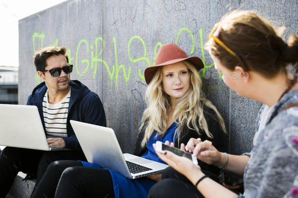 Friends talking while doing freelance work outdoors Stock Photo by ...