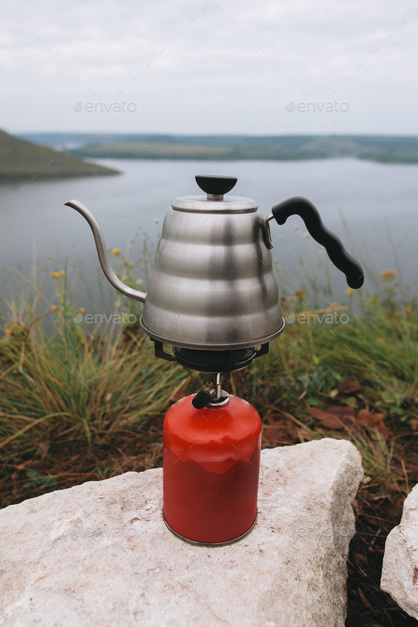 Steel kettle boiling on gas primus, making hot drink at picnic outdoors ...