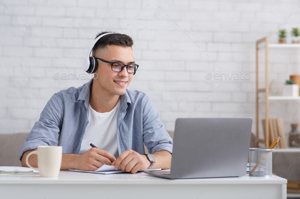 Modern education online. Smiling guy in glasses and headphones watching ...