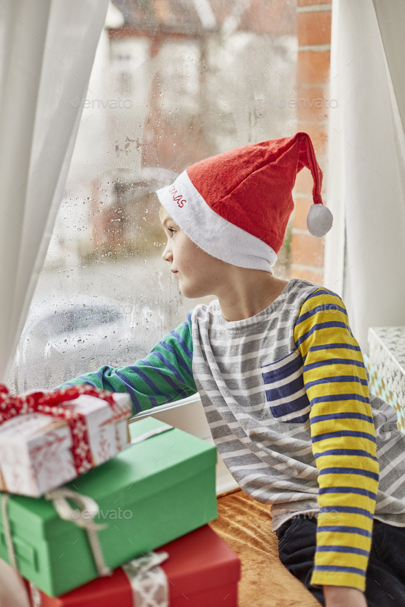 Christmas morning in a family home. A boy in a Santa hat looking out of ...
