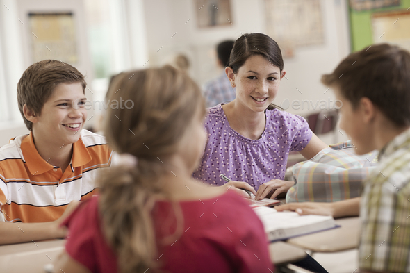 A group of students seated at a desk in a lesson talking to each other ...