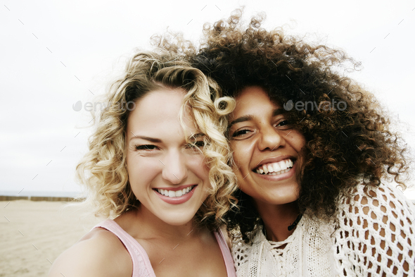 Portrait of two smiling young women with blond and brown curly hair ...