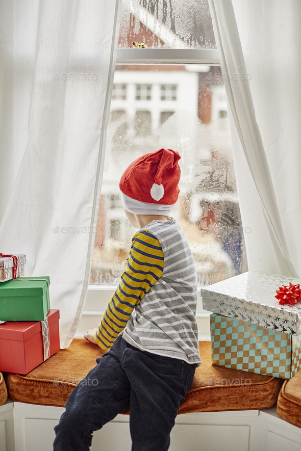 Christmas morning in a family home. A boy in a Santa hat looking out of ...