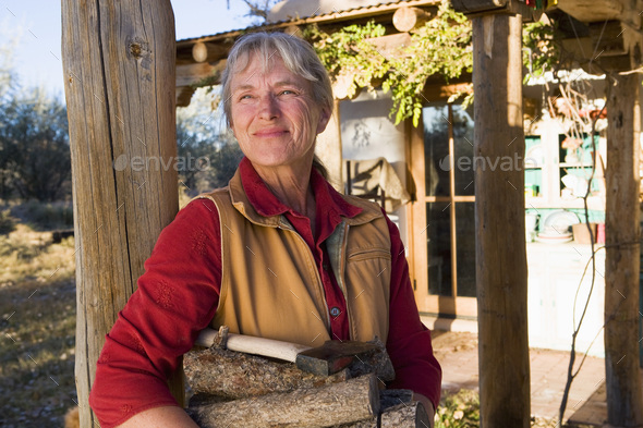 Mature woman at home on her property in a rural setting carrying logs ...