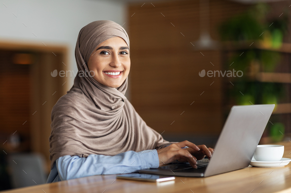 Cheerful muslim lady in hijab working online at cafe Stock Photo by ...