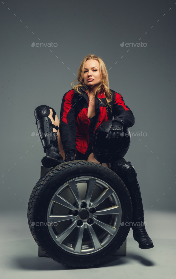 Female in motorcycle uniform posing with car wheel. Stock Photo by fxquadro