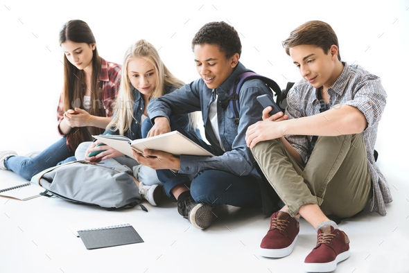 multiethnic students doing homework while friends using smartphones ...