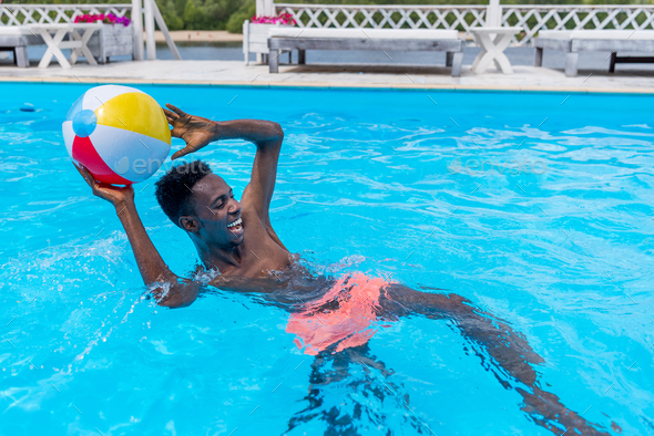 Young happy african american man playing with ball in swimming pool ...