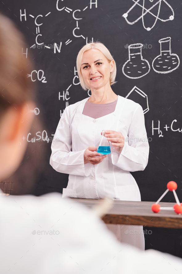 Smiling teacher of chemistry in whitecoat holding tube with liquid ...