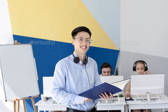 Happy Asian male helpdesk operator in headset holding documents at ...