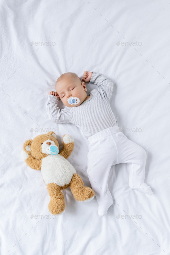 overhead view of cute baby with pacifier sleeping on bed with teddy ...