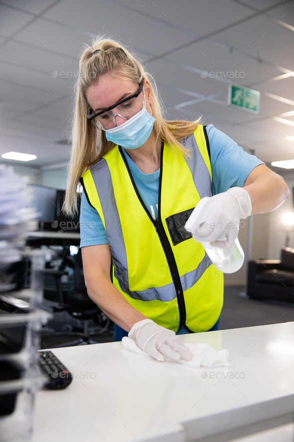 Woman wearing hi vis vest and face mask cleaning the office using ...