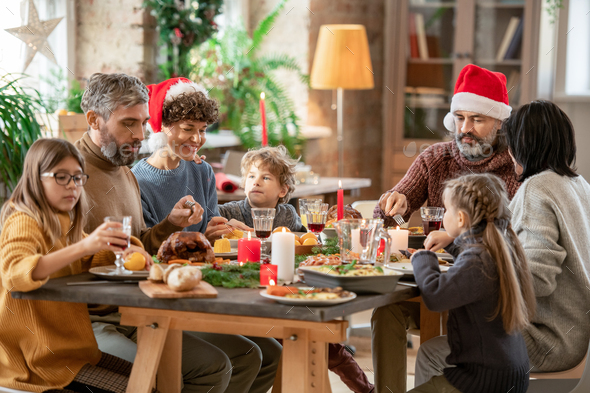 Contemporary large multi-generation family sitting by served festive ...