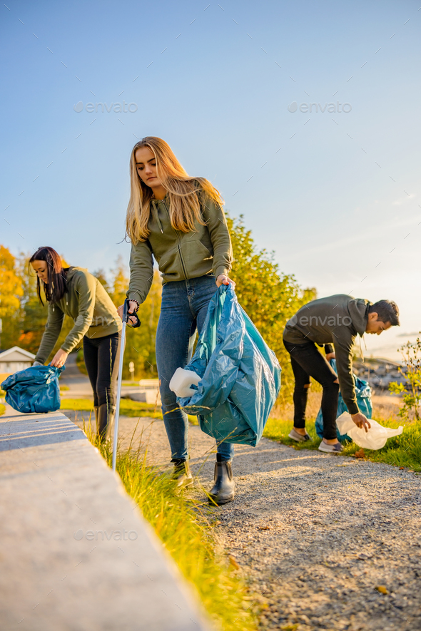 Young volunteers picking up garbage in bag at park Stock Photo by kjekol