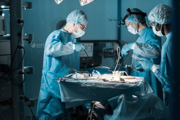 side view of multiethnic surgeons operating patient in operating room ...