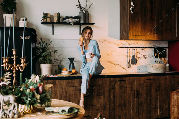 Young lady with croissant in hand chilling in the kitchen Stock Photo ...