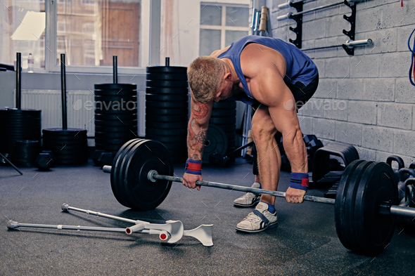 Bodybuilder with injured leg holds barbell. Stock Photo by fxquadro