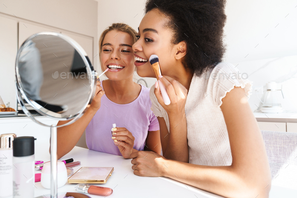Beautiful multicultural girls smiling while doing makeup together Stock ...