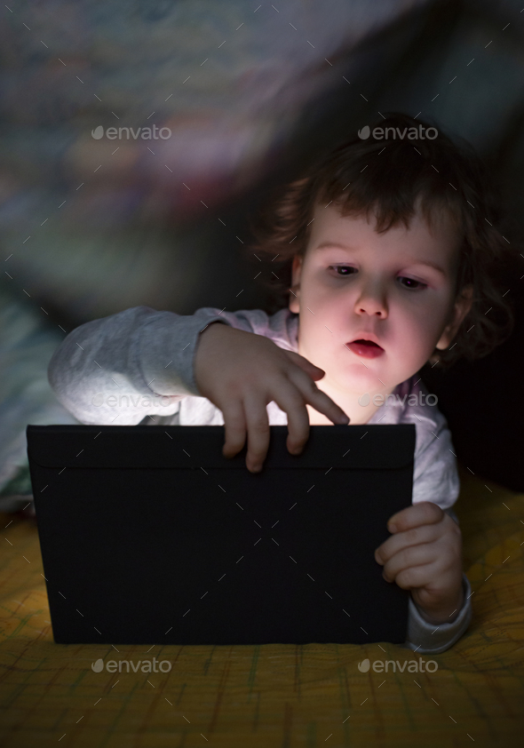 Little girl watching her tablet in the bed. Illuminated child face from ...
