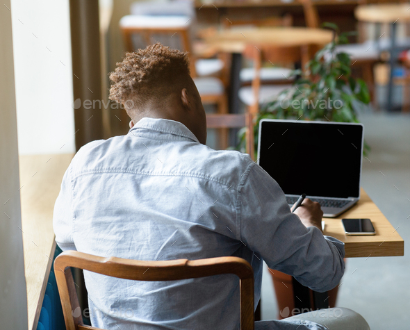Back view of young black male student studying online on laptop at city ...