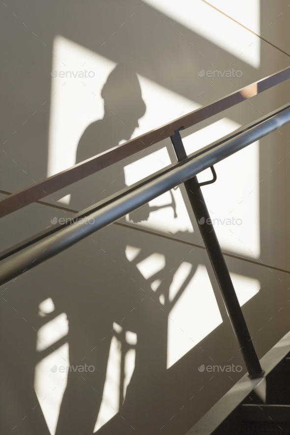 Shadow of a construction worker walking up stairs on wall with handrail ...