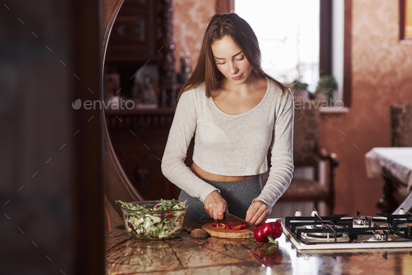 Pretty young woman standing in the modern kitchen near gas stove and ...
