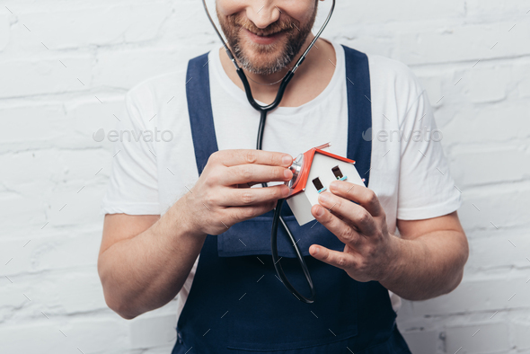 partial view of male handyman checking house figure by stethoscope ...