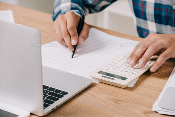 partial view of businessman making calculations at workplace with ...