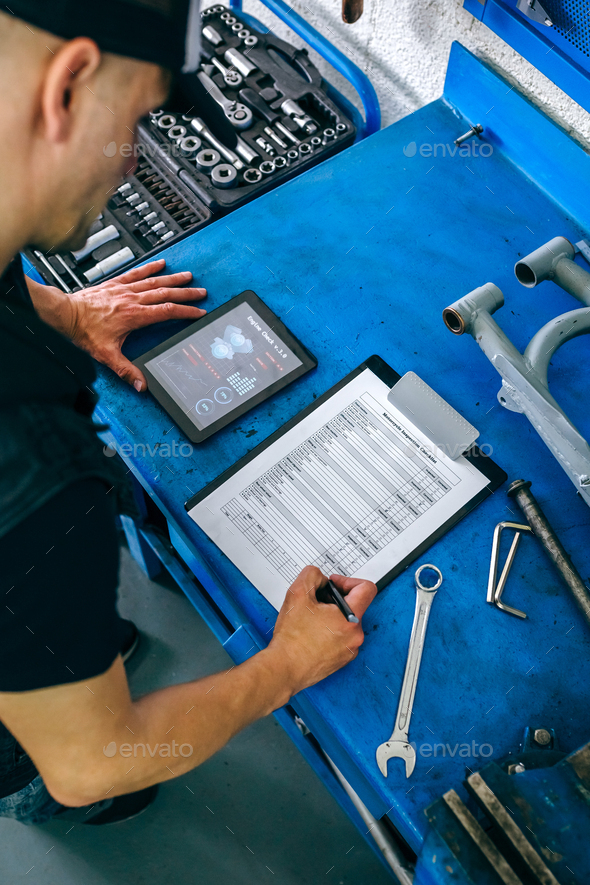 Mechanic using tablet app and taking notes Stock Photo by davidpereiras