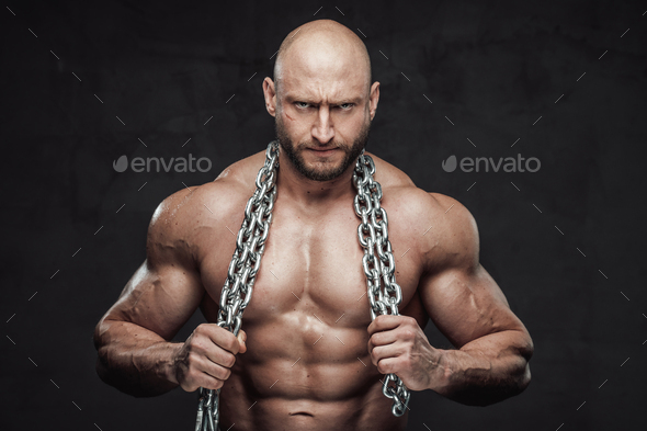 Serious and handsome guy poses in dark background with heavy chains ...