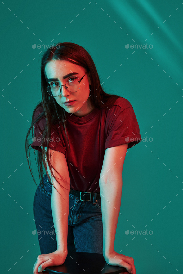 Leans on chair. Studio shot indoors with neon light. Portrait of ...