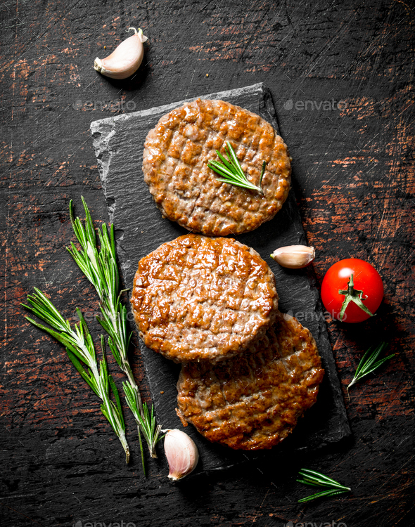 Cutlets on a black stone Board with pieces of garlic,rosemary and ...