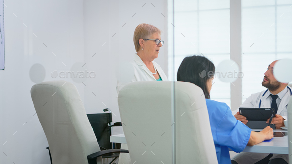 Medical team sitting and discussing at table in hospital meeting office ...