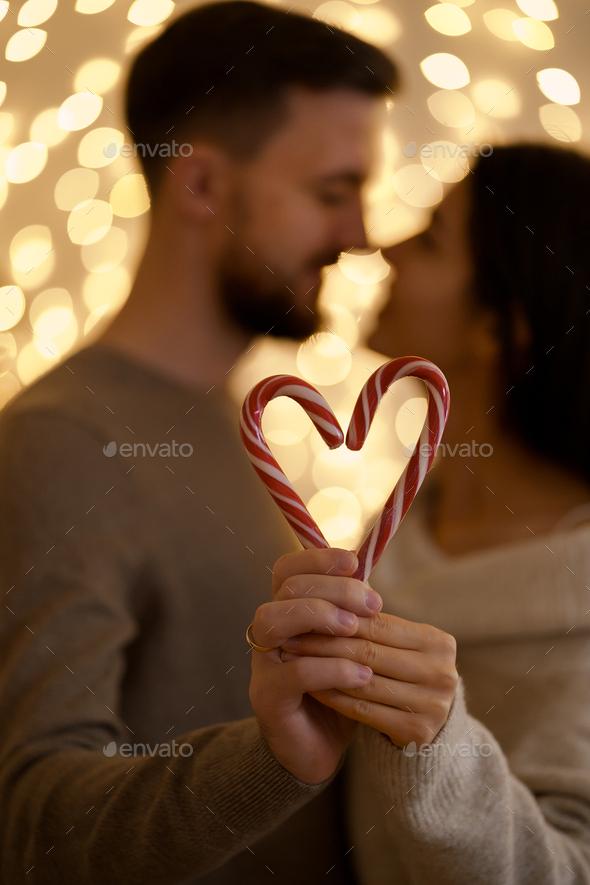 couple kissing and showing the heart-shaped figure of candy canes ...
