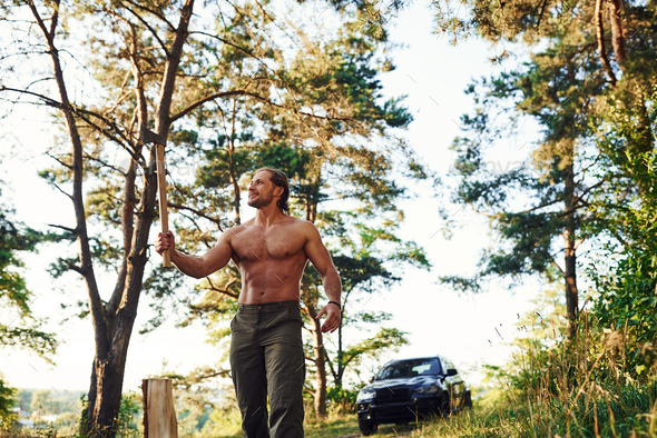 Handsome shirtless man with muscular body type is in the forest at ...