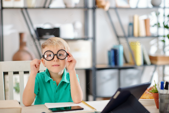 Boy putting on glasses with thick lenses Stock Photo by DragonImages