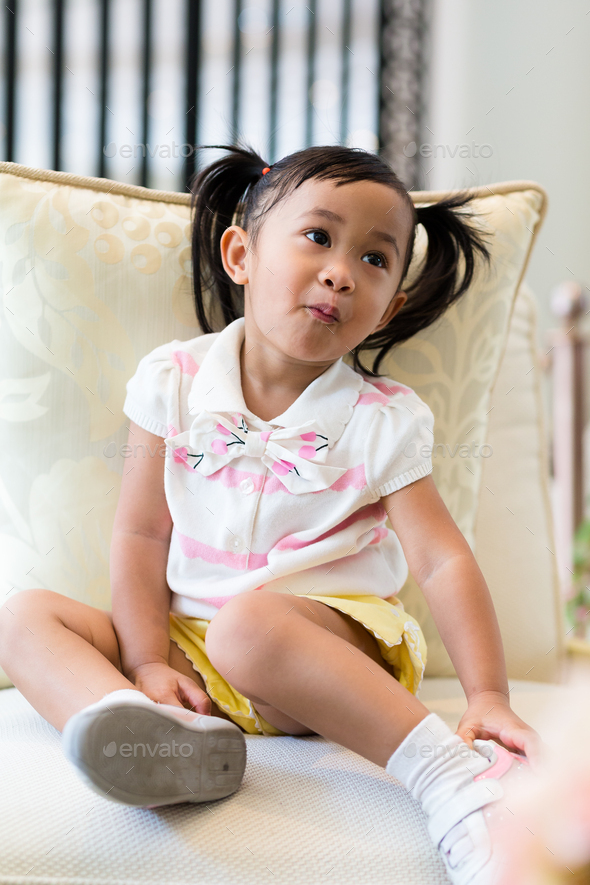 Cuty little girl with candy in mouth and sitting on sofa Stock Photo by ...
