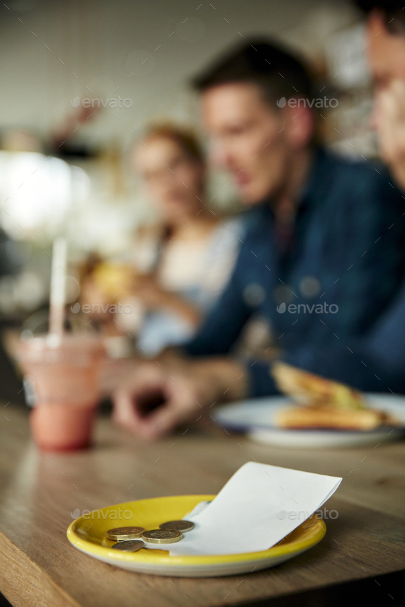 People at a cafe table, a saucer with till receipt and cash payment ...