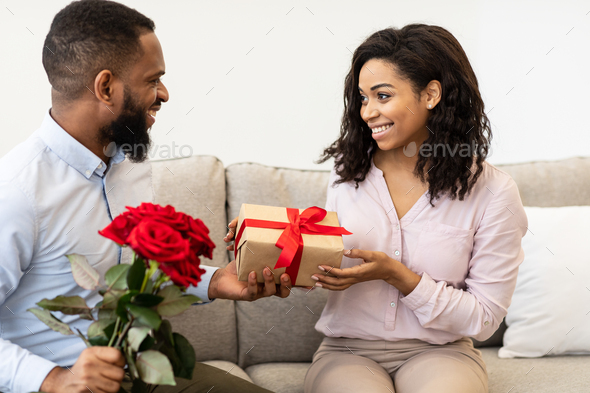Happy black guy giving red roses and box to woman Stock Photo by ...
