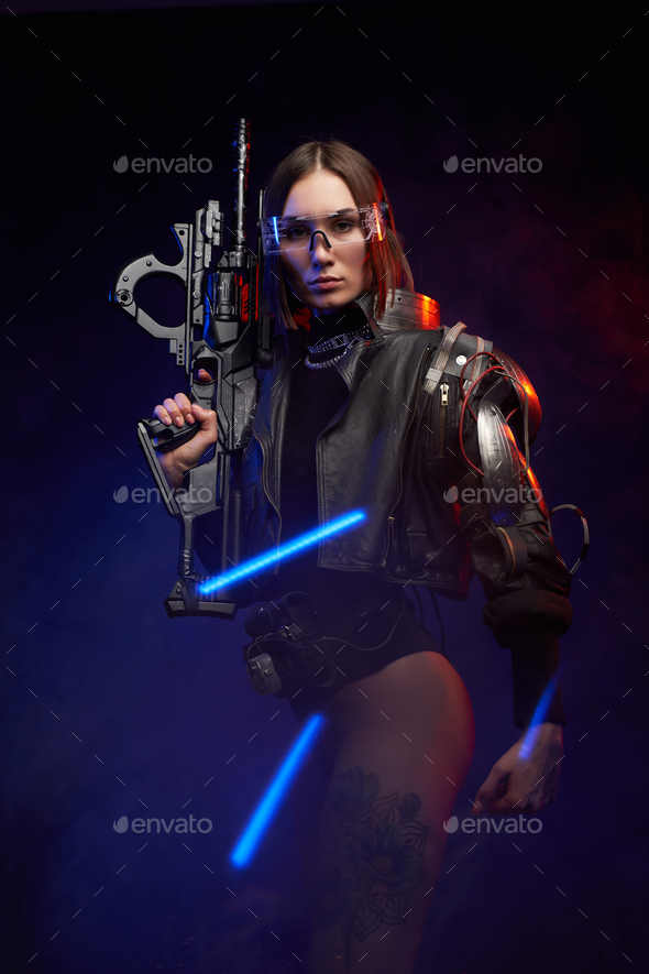 Futuristic female agent armed with rifle posing in dark background ...